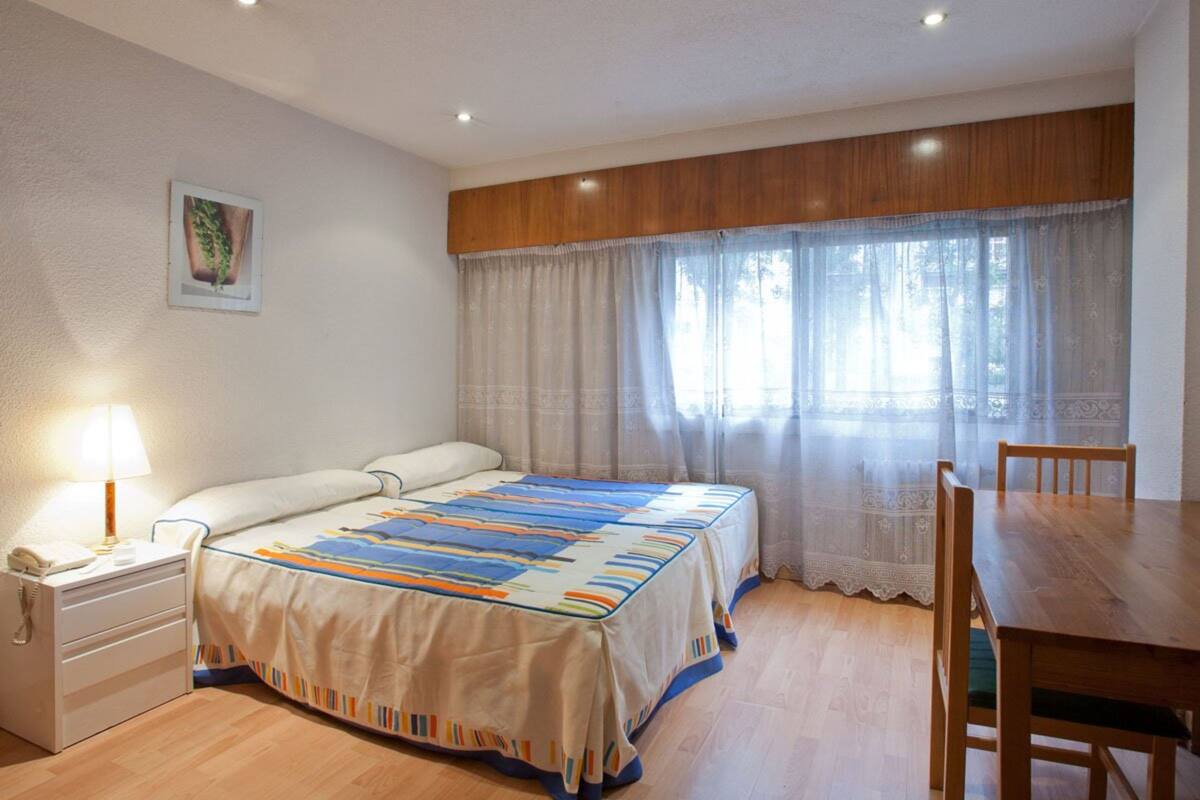 Quarto com cama, mesa de cabeceira, luminária e uma mesa de jantar de madeira com cadeiras.