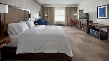 Quarto de hotel com uma cama grande, uma escrivaninha com computador, uma televisão e uma cadeira.