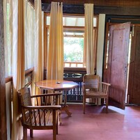 Uma área de refeições com mesa redonda e duas cadeiras, uma porta de madeira e uma janela com cortinas.