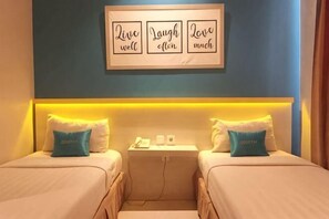 Quarto de hotel com duas camas, uma mesa de cabeceira, um letreiro fixado na parede e cabeceira com iluminação integrada.