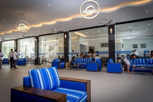 Um hall amplo com sofás listrados em azul, uma mesa de centro e ventiladores de teto.