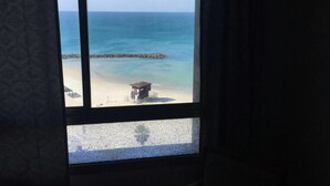 Vista pela janela de uma praia, com uma torre de salva-vidas e um molhe rochoso.