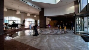 Um hall amplo com design circular no chão, grandes janelas e área de estar com mesas e cadeiras.