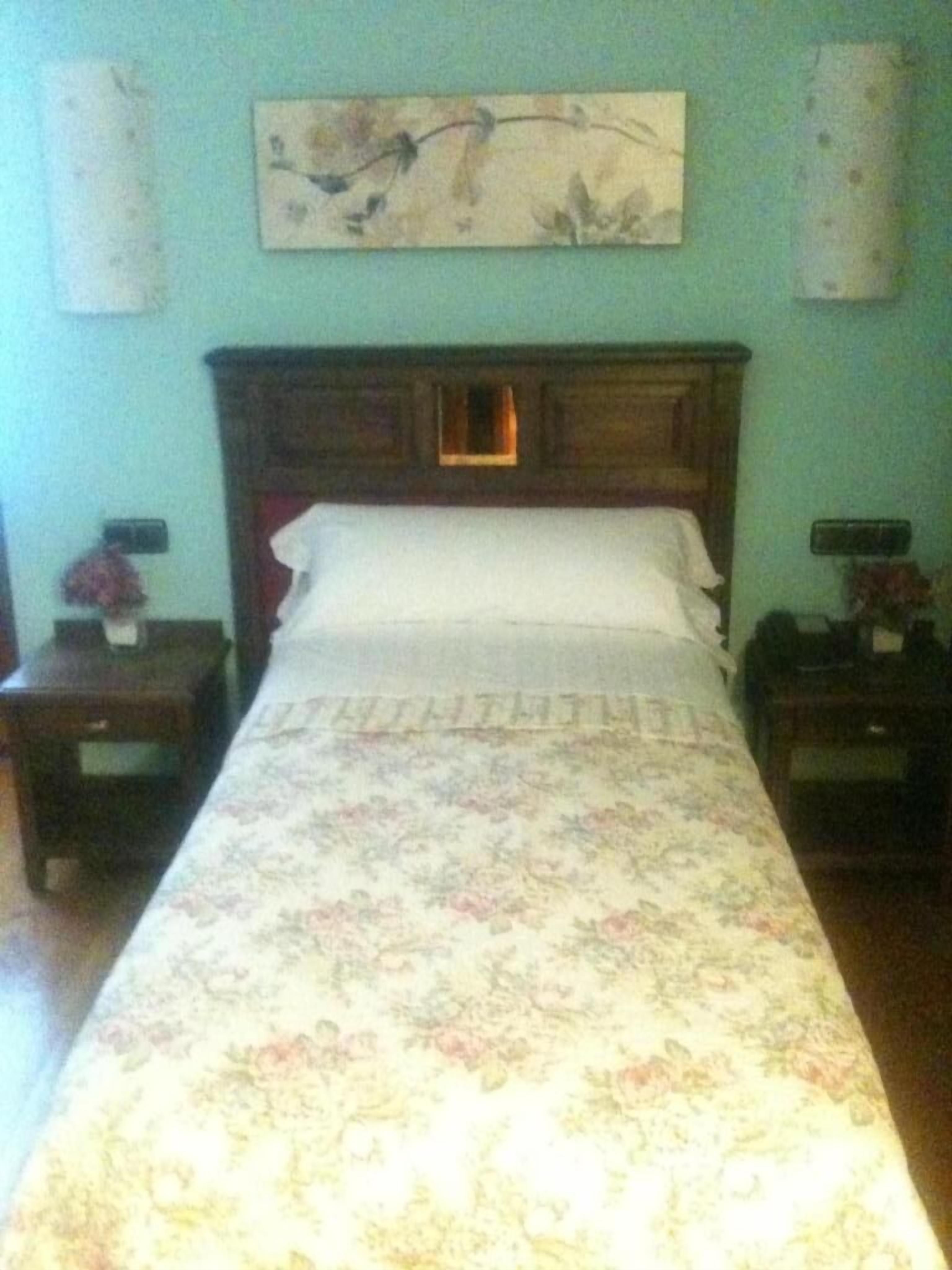 Quarto com cama grande, cabeceira de madeira, colcha estampada com flores e uma obra de arte na parede.