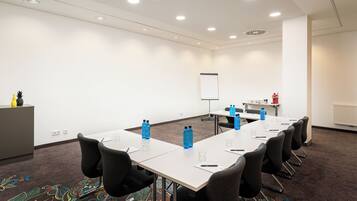 Uma sala de conferência com uma mesa comprida, cadeiras, um quadro branco e garrafas de água.