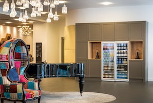 Um hall moderno com um piano preto, uma poltrona colorida e dois refrigeradores para bebidas.