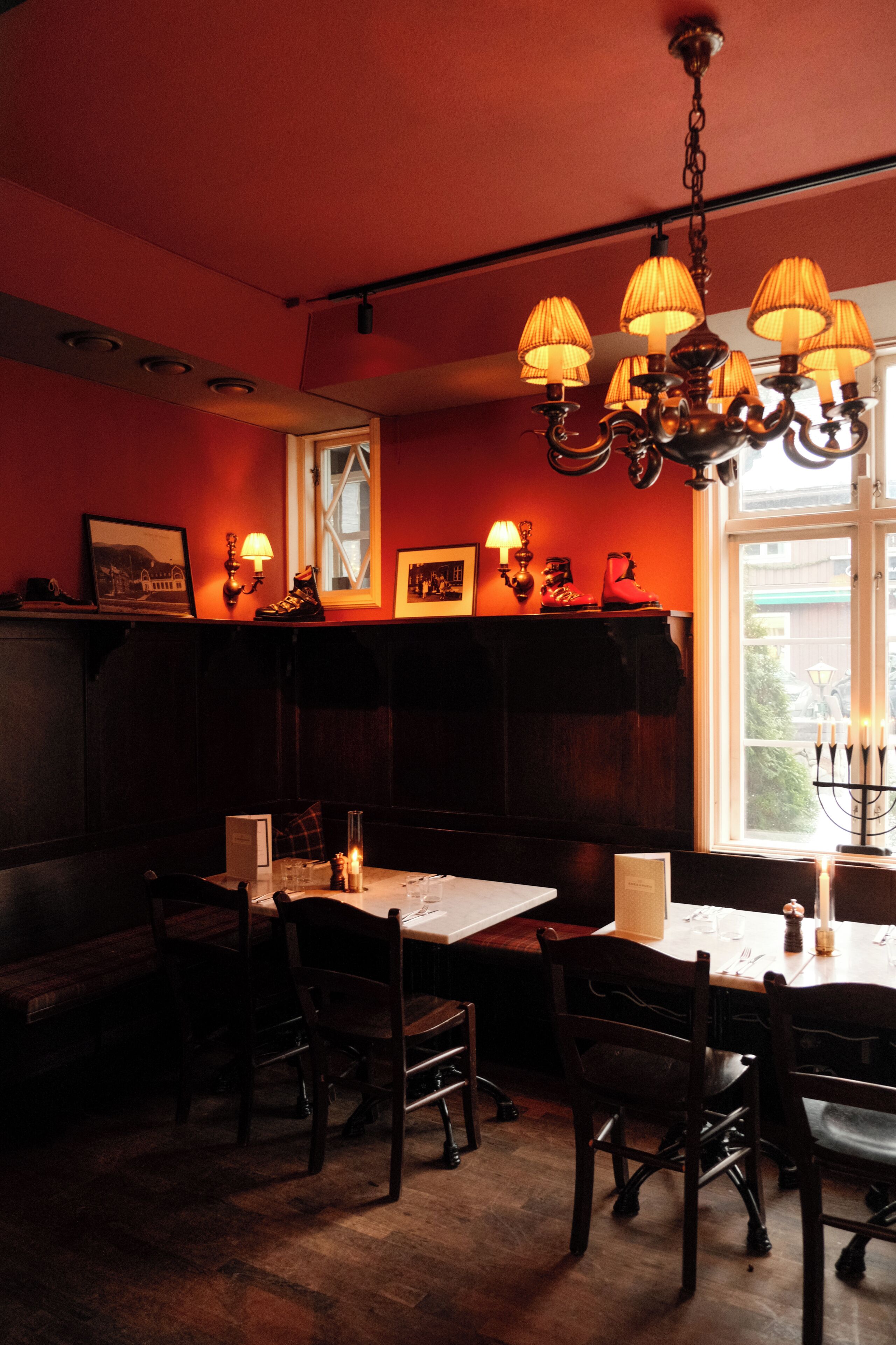 Restaurante com iluminação suave, móveis de madeira, um candelabro e luminárias nas paredes.