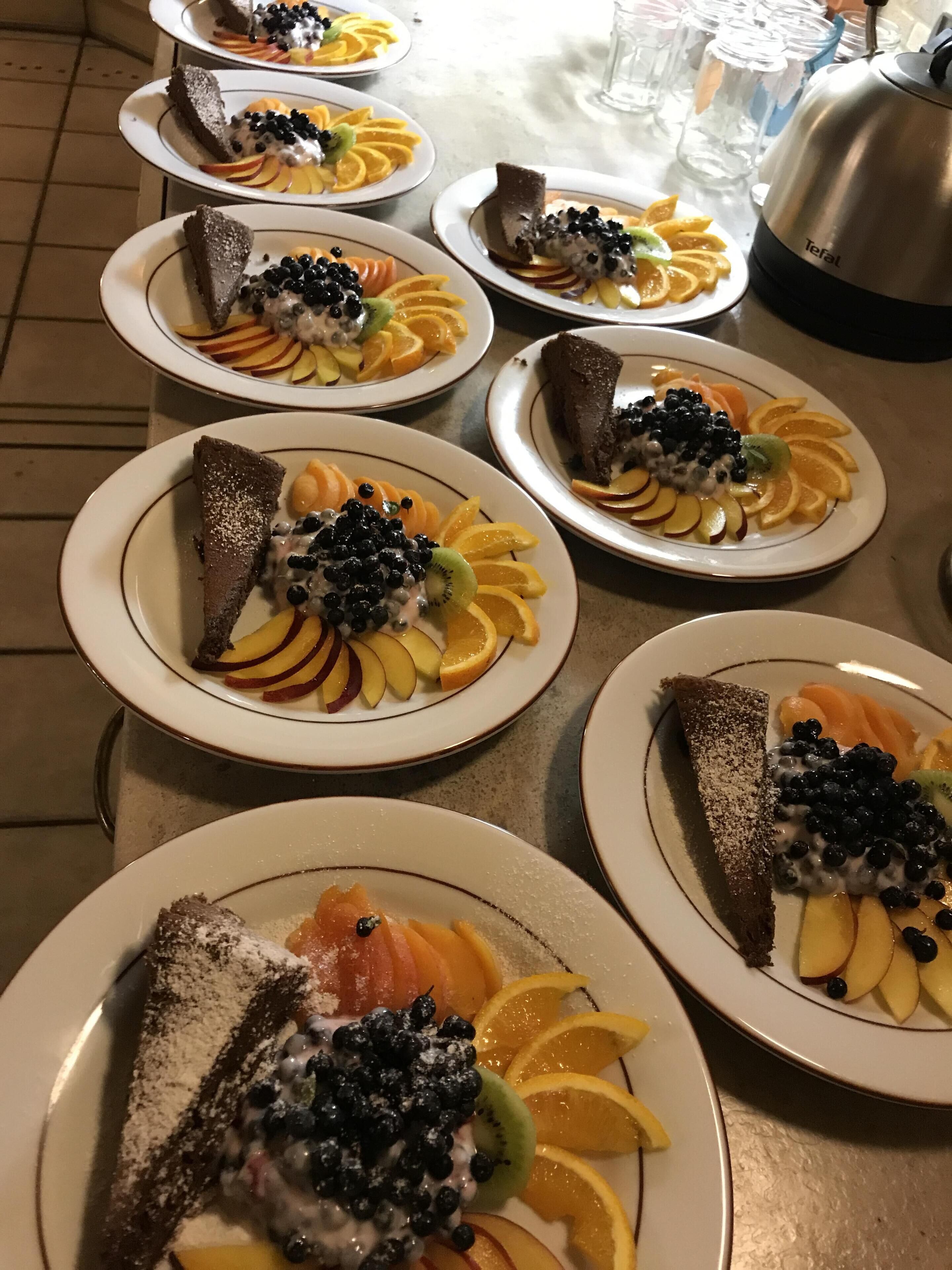 Uma mesa com várias sobremesas, incluindo fatias de bolo, kiwi, laranja e mirtilos.