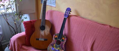 Um sofá rosa com duas guitarras, uma acústica e outra elétrica, e um abajur sobre uma mesa.
