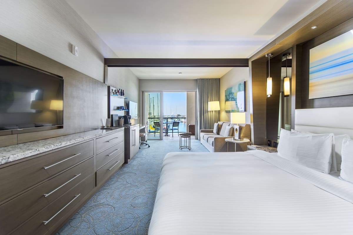 Quarto de hotel com uma cama grande, televisão, escrivaninha e varanda com vista.