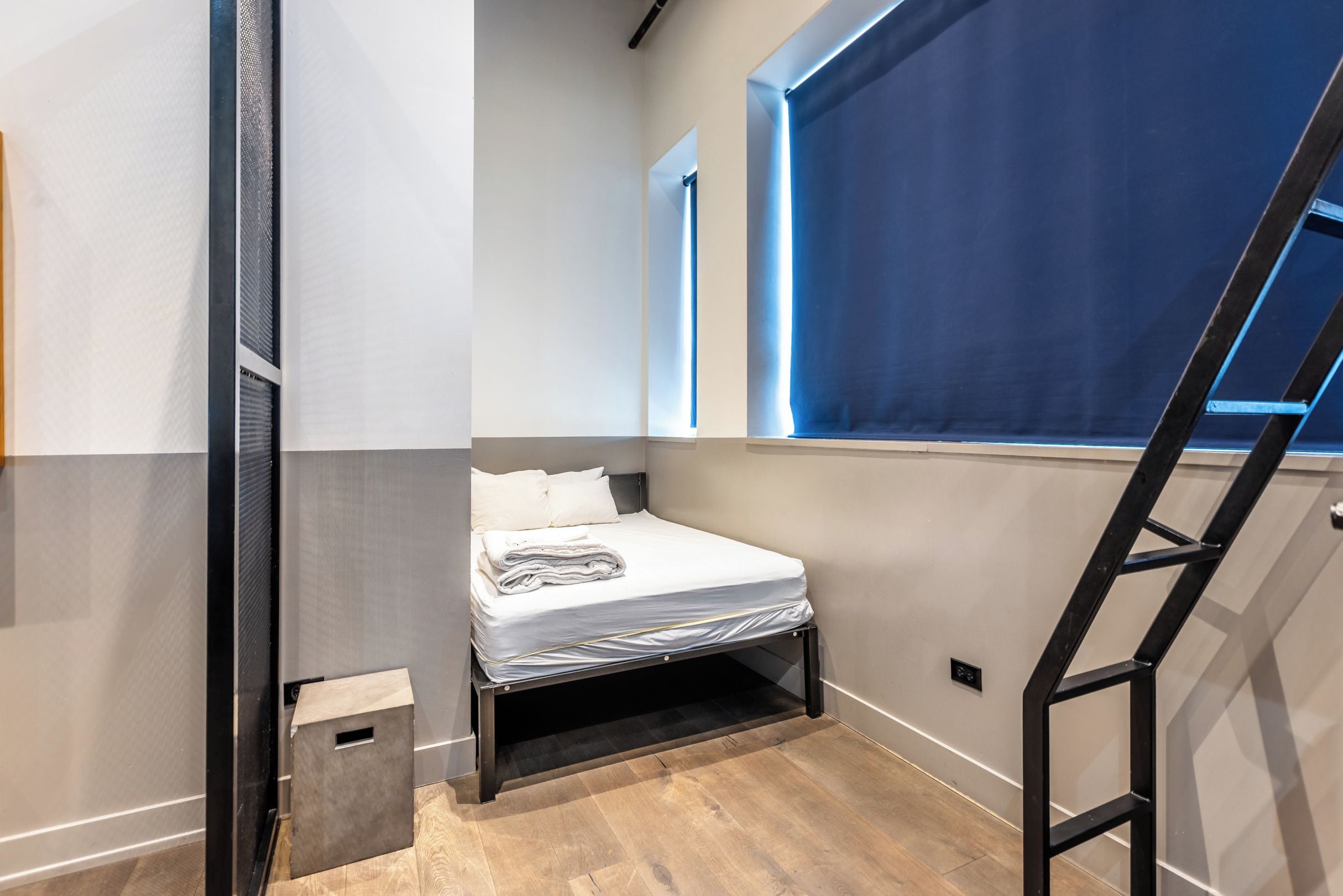 Quarto compacto com uma cama, um pequeno armário e uma janela com persianas.
