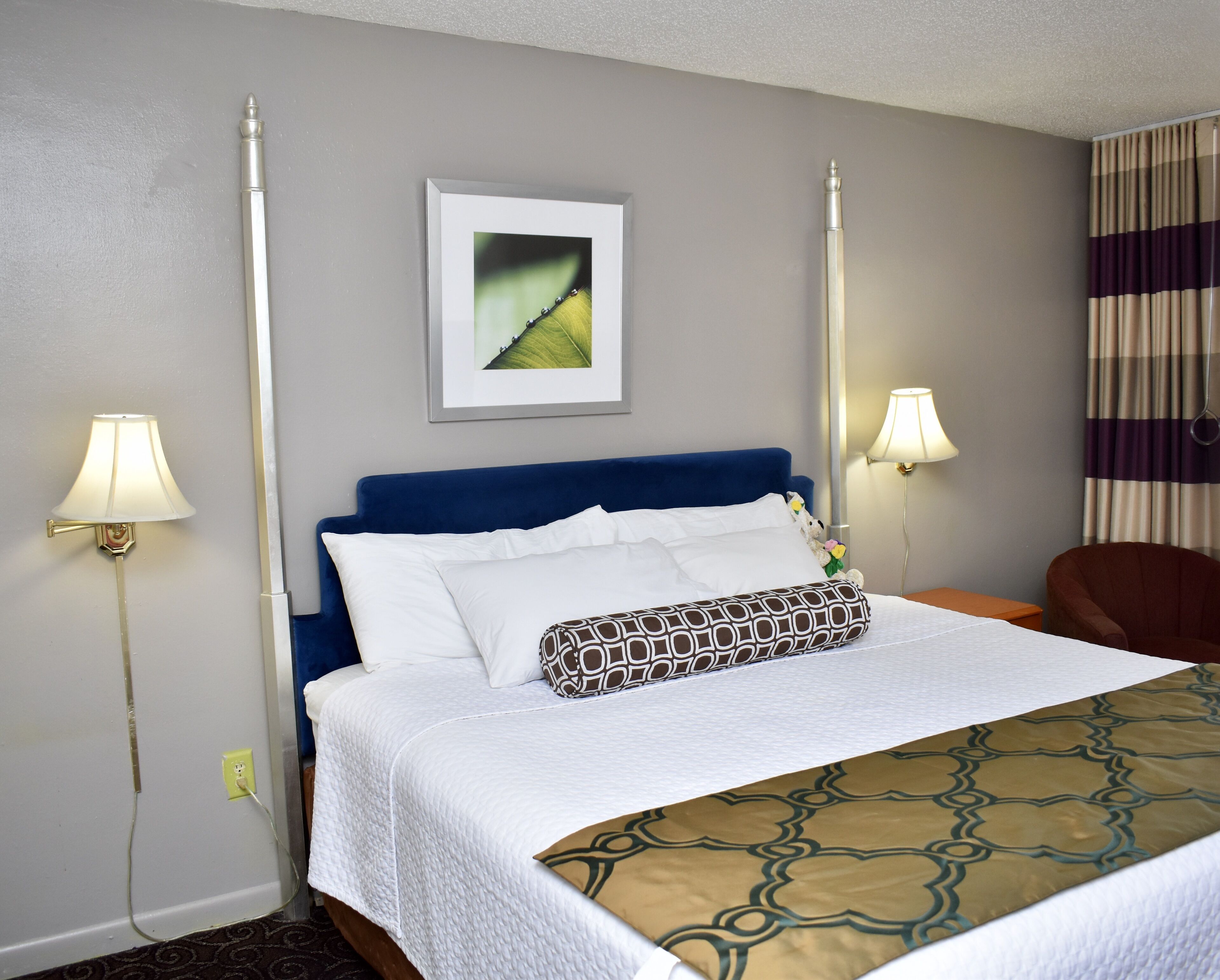 Quarto de hotel com uma cama grande, duas luminárias de cabeceira, um quadro na parede e uma cortina listrada.