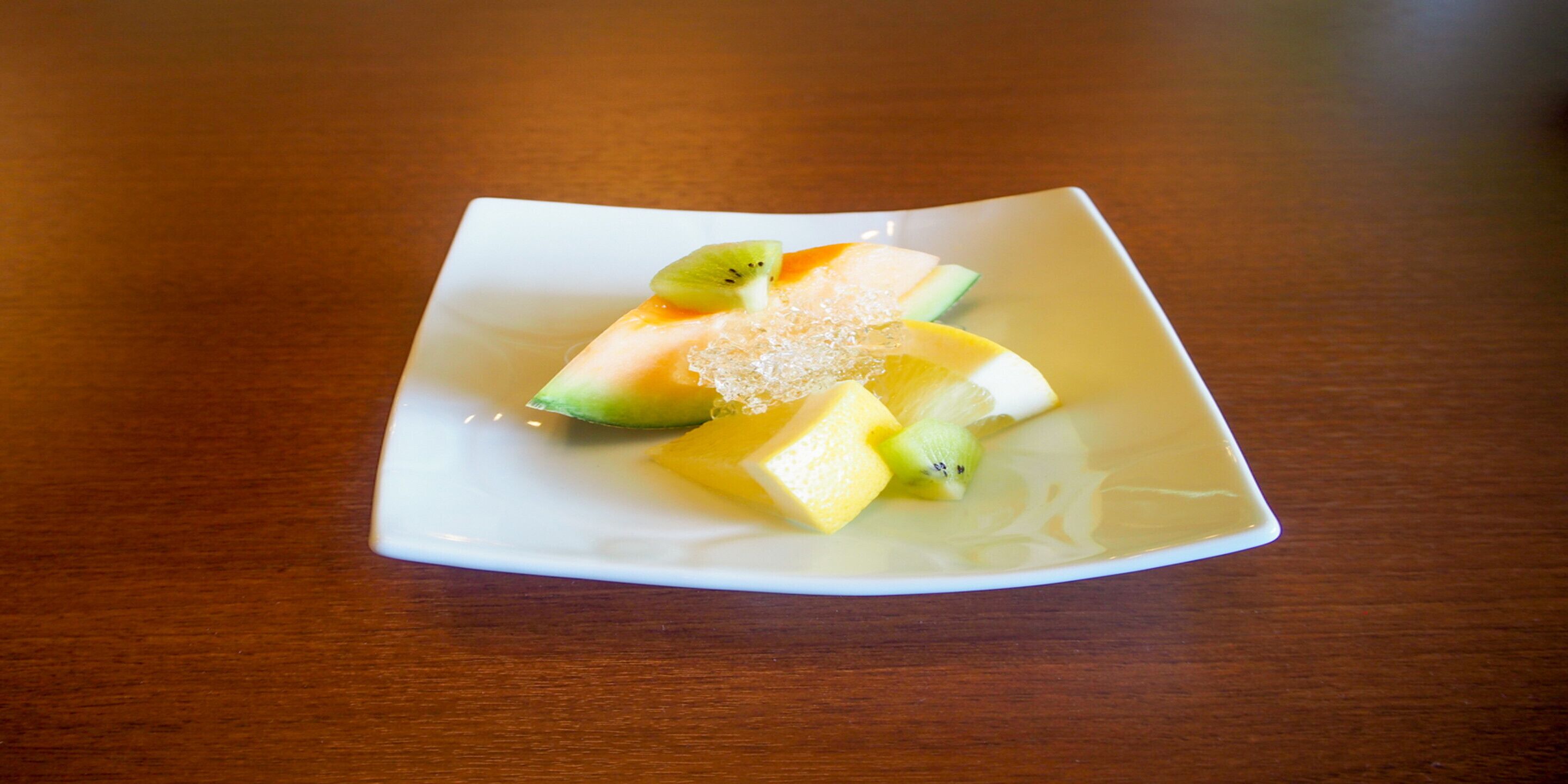 Prato quadrado branco com fatias de fruta sobre mesa de madeira.