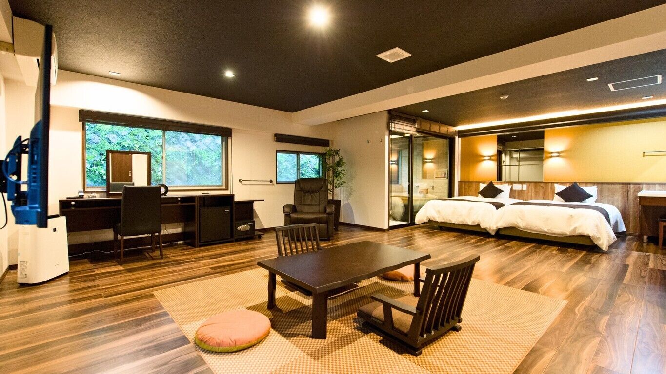 Quarto de hotel moderno com escrivaninha, cadeira, cama e janelas amplas.