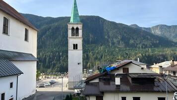 Uma cidade com uma torre de igreja imponente, carros estacionados e montanhas ao fundo.