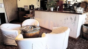 Quarto com área de bar, poltronas brancas, uma pequena mesa com um jornal e uma planta em vaso.