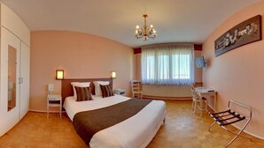 Quarto de hotel com uma cama grande, escrivaninha, cadeira, televisão e um candelabro.