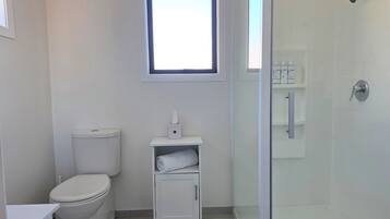 Casa de banho moderna com sanita, cabine de duche em vidro e um pequeno armário com produtos de higiene pessoal.