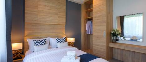 Quarto de hotel com uma cama grande, cabeceira de madeira, guarda-roupa, espelho e mesa de cabeceira com abajur.
