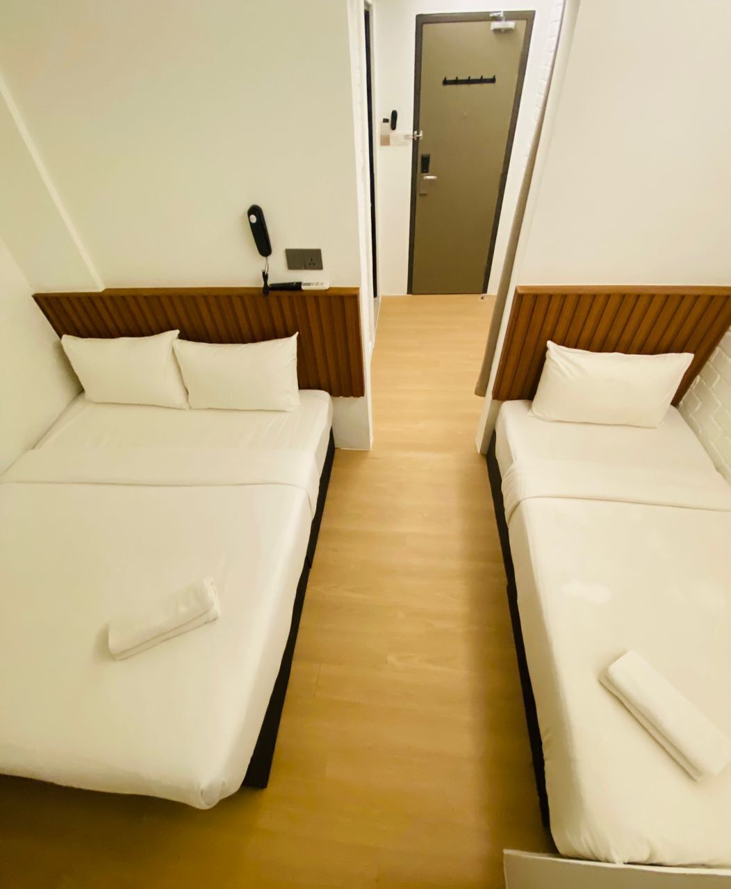 Quarto de hotel com duas camas, uma cabeceira de madeira, mesa de cabeceira com telefone e uma porta ao fundo.