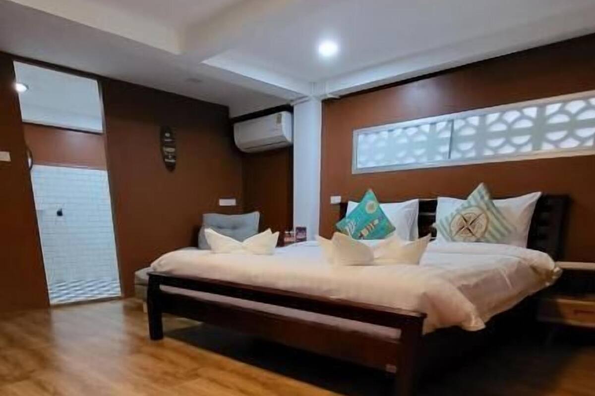 Quarto de hotel com piso de madeira, cama com roupa de cama branca e janela com um painel decorativo.