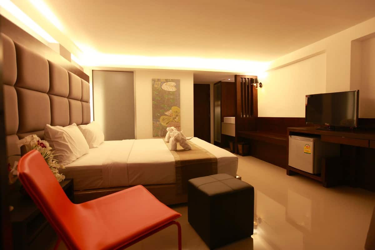 Quarto de hotel com cama, uma cadeira vermelha, uma mesa pequena, televisão e frigorífico.