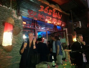Restaurante com letreiro de neon, mesas ao ar livre e fachada de pedra.