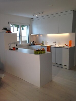 Cozinha moderna com ilha central, armários brancos e janela que proporciona iluminação natural.