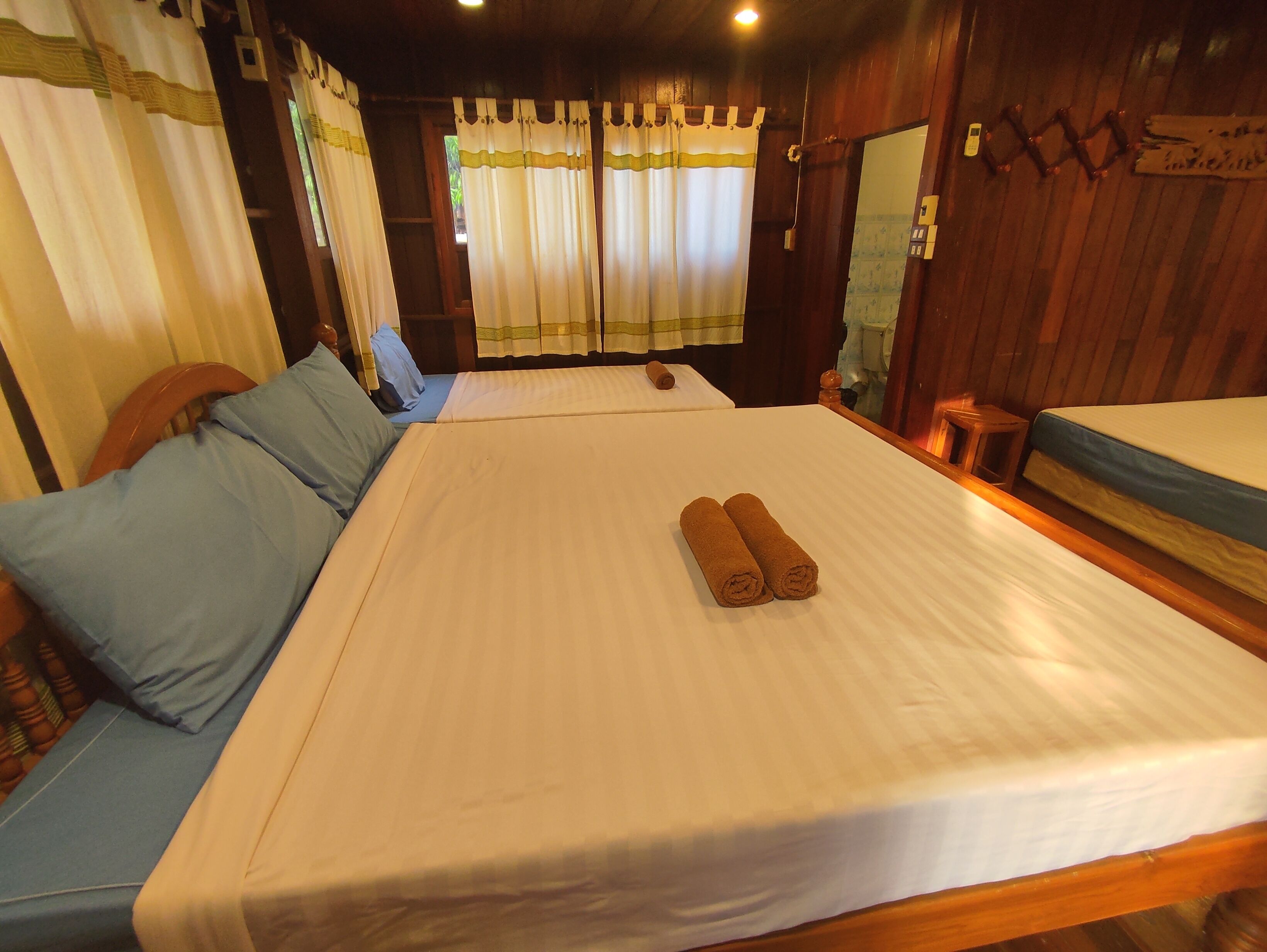 Quarto com duas camas, cada uma com cabeceira de madeira, uma cama grande no centro com toalhas enroladas e uma janela com cortinas.