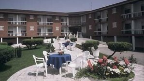 Um pátio com área de estar externa, um pequeno jardim e um edifício de vários andares com varandas.