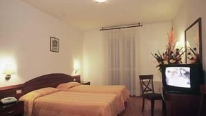 Quarto de hotel com cama de casal, mesa de cabeceira com abajur, televisão e uma cadeira.