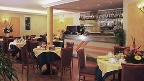 Restaurante com várias mesas e cadeiras, área de bar e balcão com caixa registradora.
