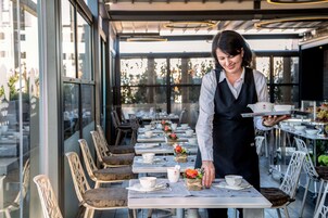 Um restaurante com mesas ao ar livre, toalhas brancas e um garçom servindo pratos.