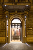 A entrada do hotel Monti Palace, com uma porta em arco, trabalhos em pedra ornamentados e uma placa acima da entrada.