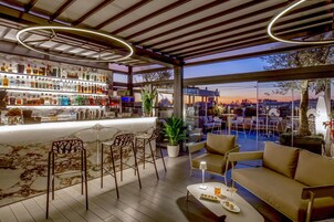 Uma área de bar moderna com bancada de mármore, várias garrafas de bebidas alcoólicas e um espaço de estar com sofá e cadeiras.