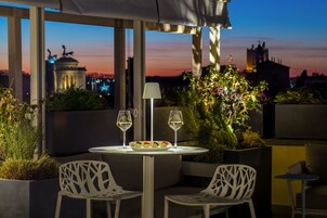Área de refeições no terraço com uma mesa posta para dois, duas taças de vinho e um prato de comida.
