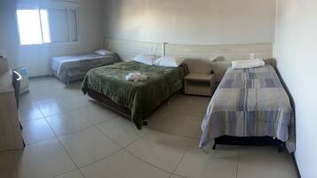 Quarto de hotel com duas camas de solteiro, uma mesa de cabeceira com abajur e uma janela com persianas.