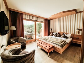 Quarto com uma cama grande, área de estar com um banco, televisão e vista para o exterior.