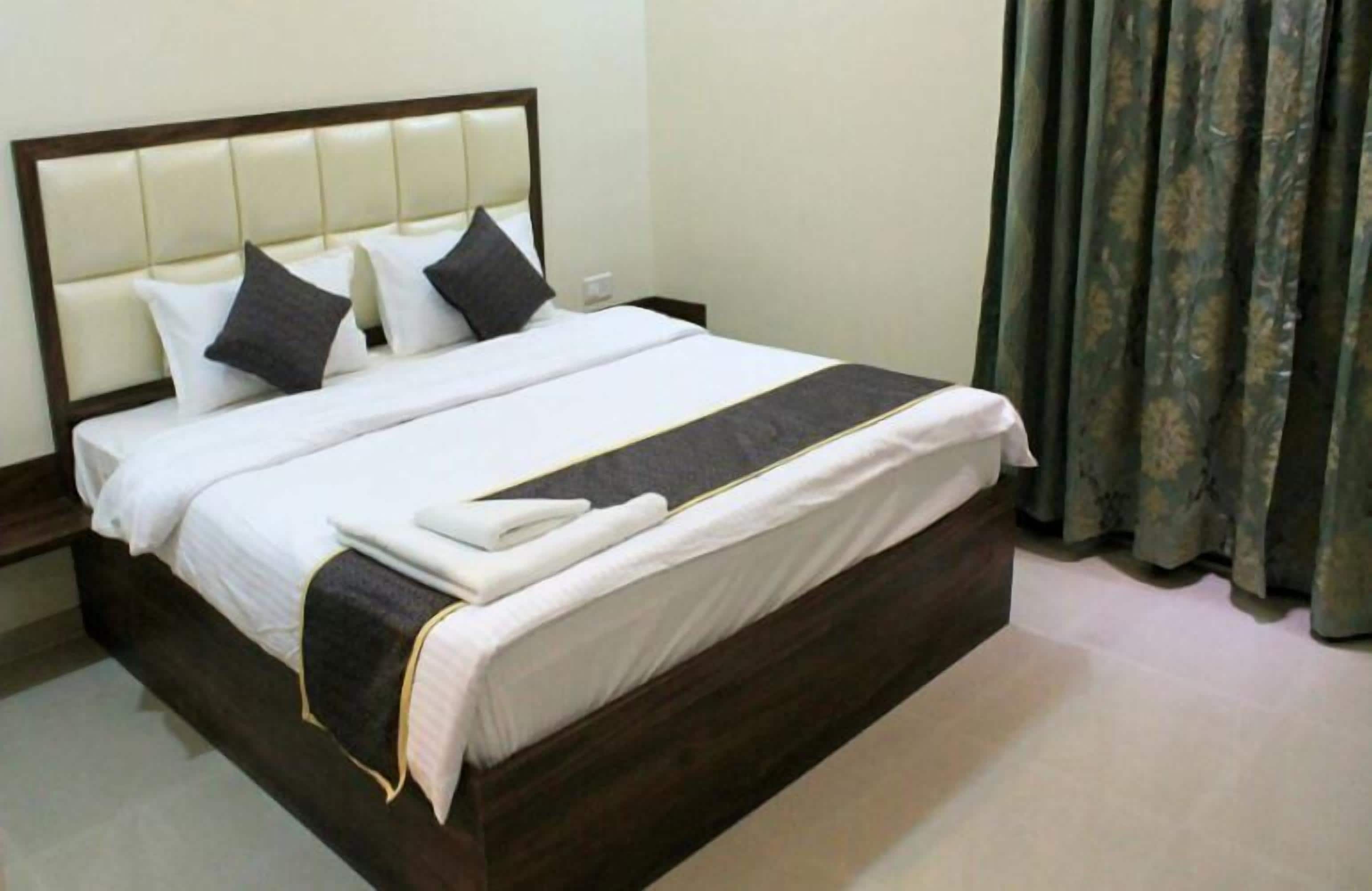 Cama bem arrumada com estrutura de madeira escura e roupa de cama branca, incluindo travesseiros e um cobertor.