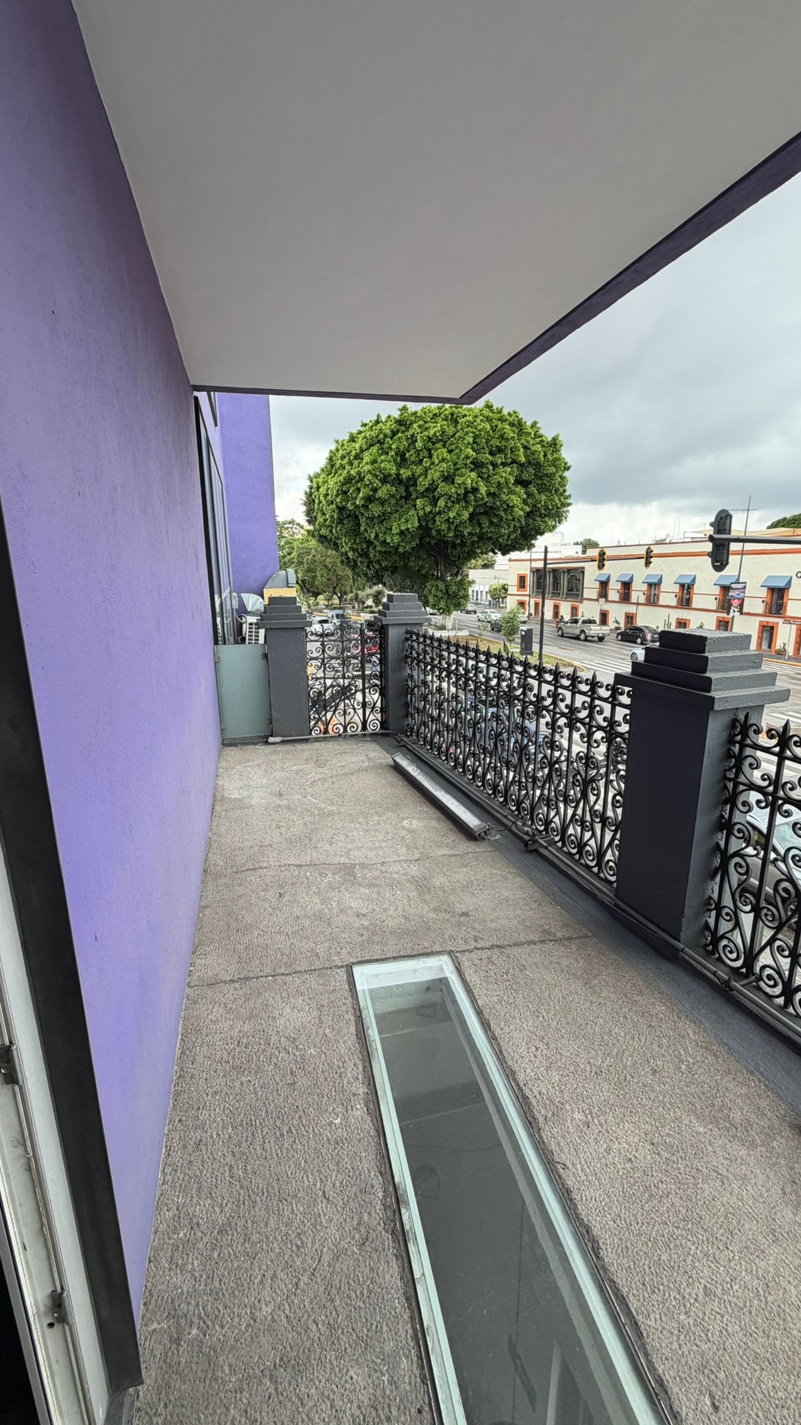 Varanda com grade de metal, porta de vidro e vista para árvores e edifícios.