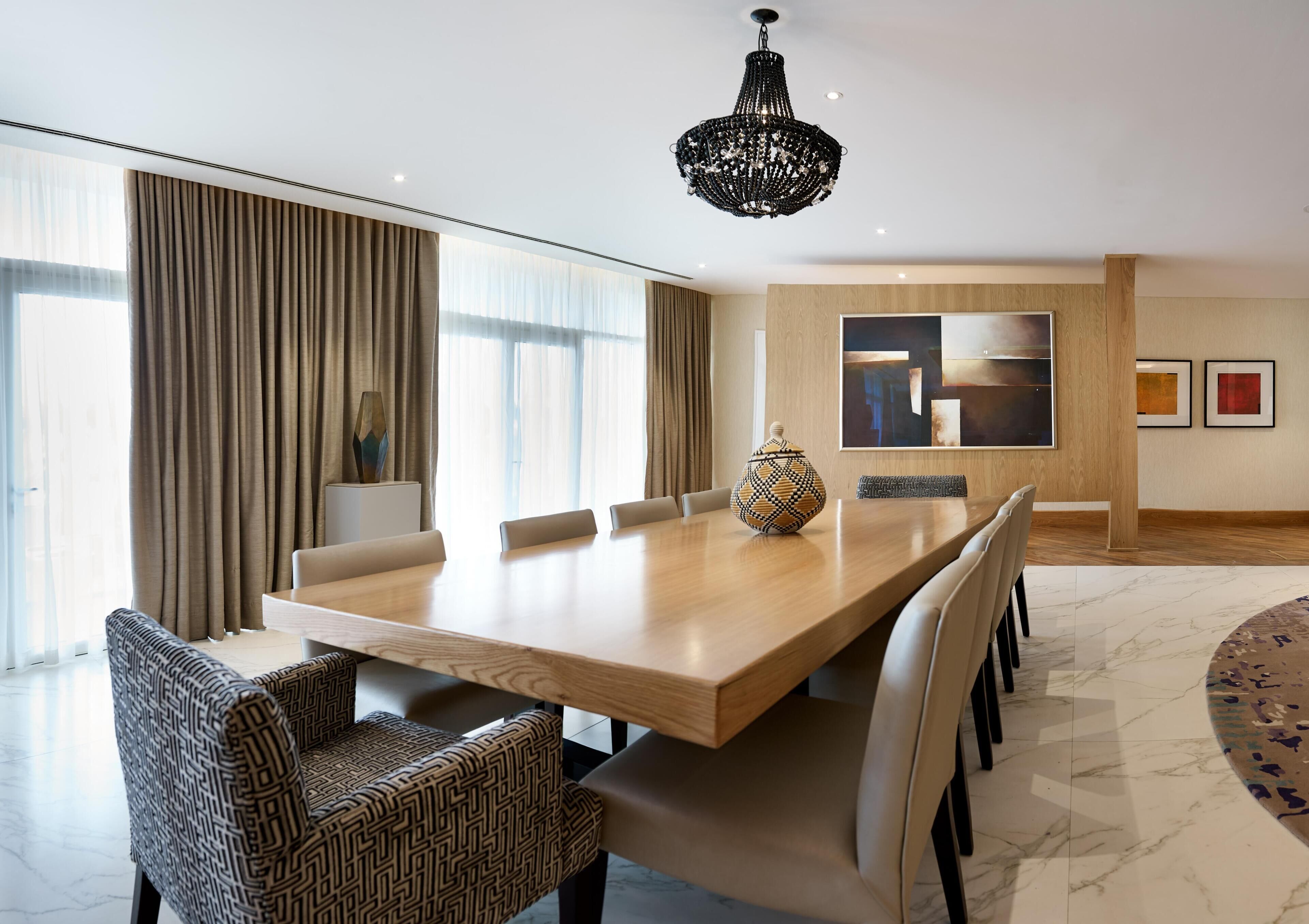 Uma sala de conferências moderna com uma grande mesa de madeira, cadeiras estampadas e um vaso decorativo.