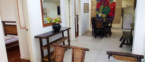 Um quarto com uma cama, uma mesa de jantar com cadeiras, um espelho e um quadro colorido na parede.