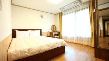Quarto de hotel com cama grande, piso de madeira, mesa de cabeceira com espelho e janela com cortinas.