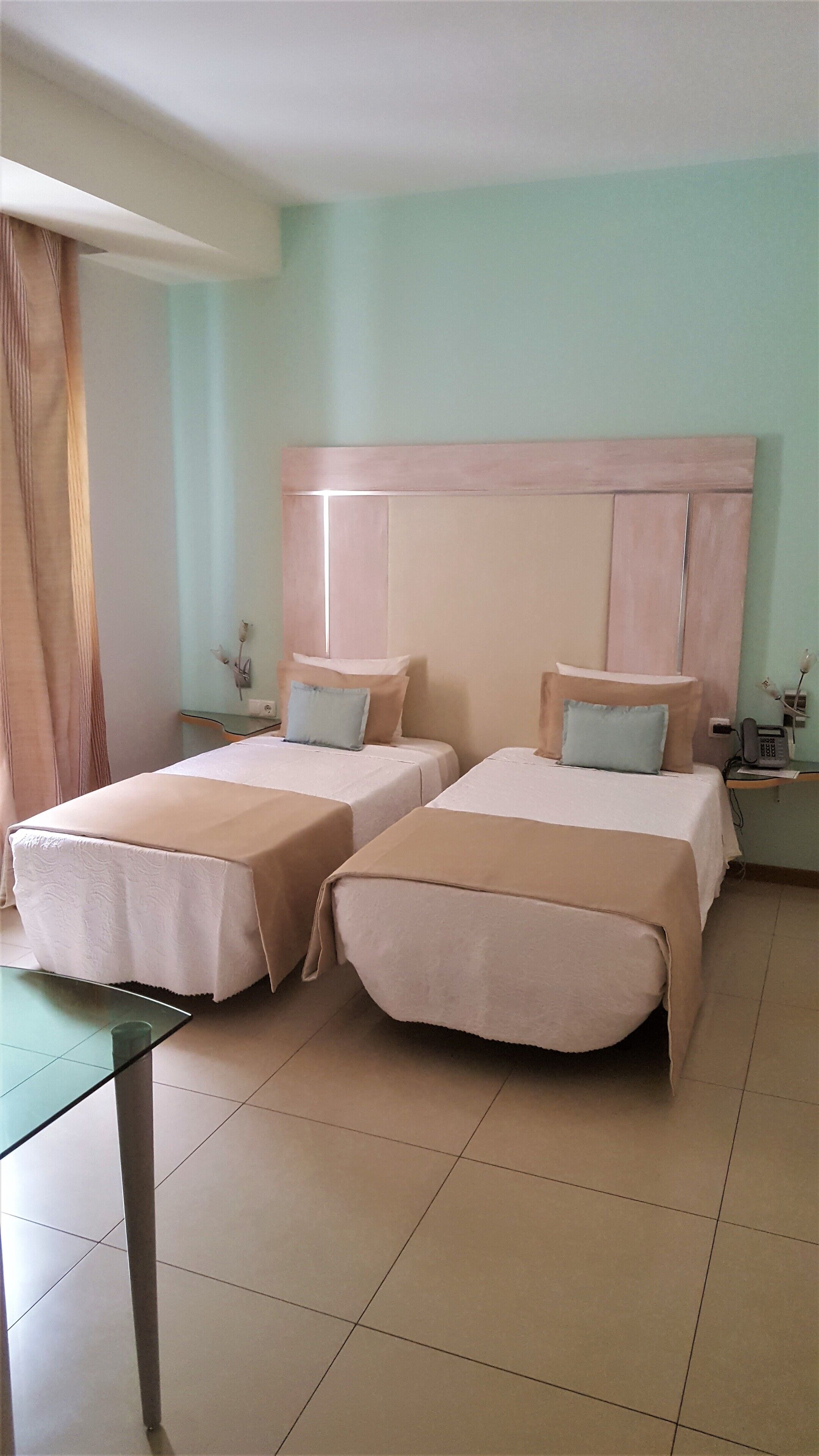 Quarto de hotel com duas camas, uma mesa de vidro e um telefone em uma mesinha de cabeceira.