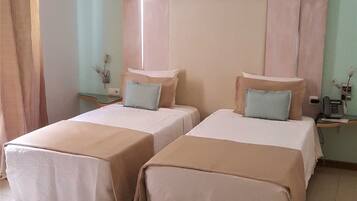 Quarto de hotel com duas camas, uma mesa de vidro e um telefone em uma mesinha de cabeceira.