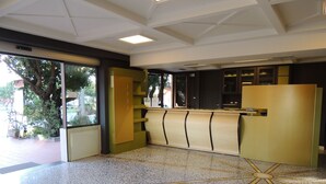 Uma área de recepção com design moderno, destacando um balcão de atendimento, uma grande janela e um piso revestido de azulejos.