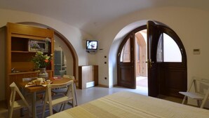 Quarto com cama, escrivaninha com cadeira, televisão e porta arqueada.
