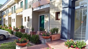 Edifício residencial com várias andares, varandas, plantas em vasos e um carro estacionado na frente.