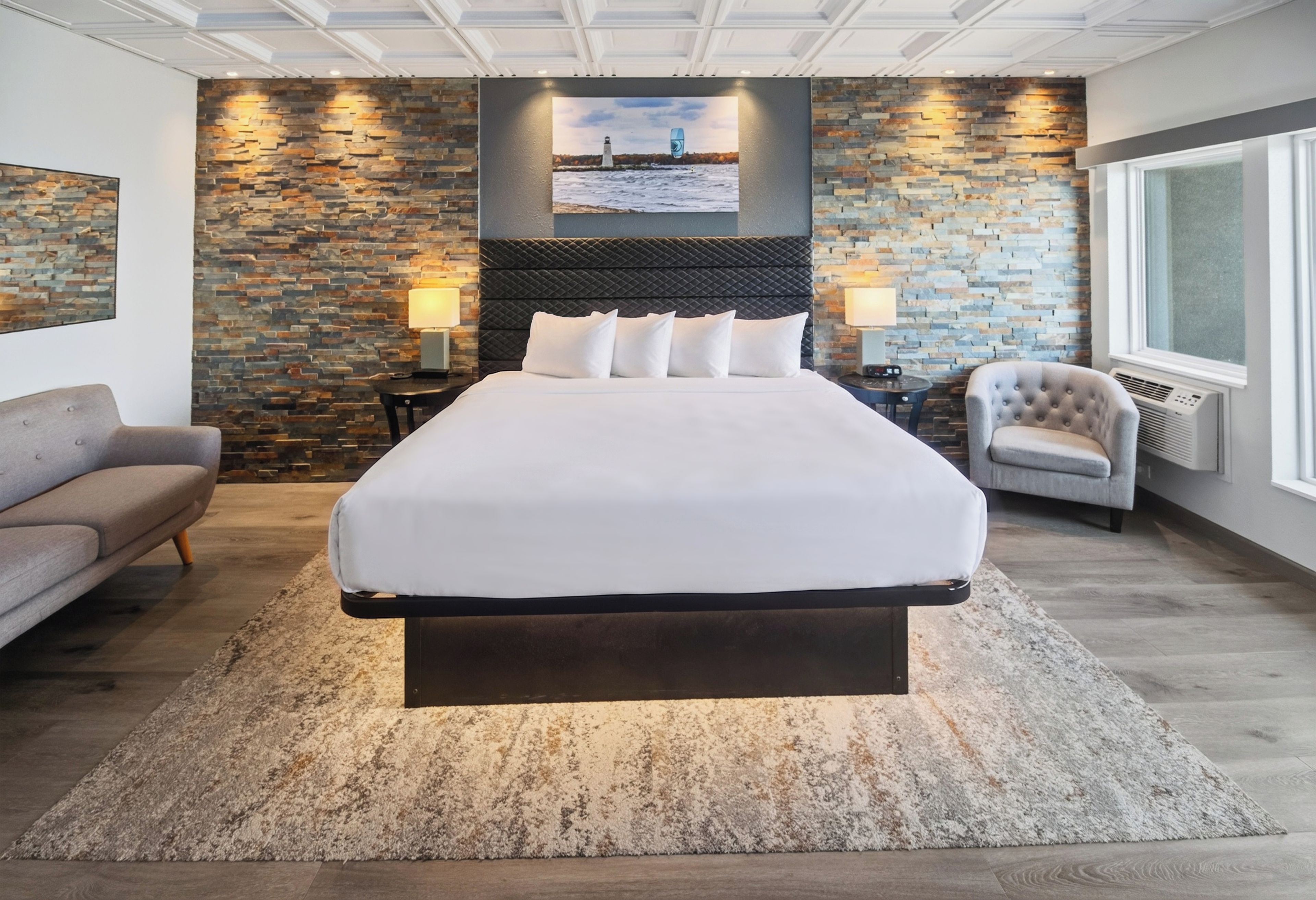 Quarto moderno com cama grande, parede de pedra e pintura de um farol.