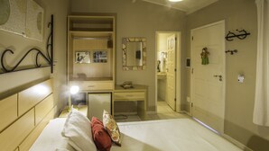 Um quarto com uma cama, uma escrivaninha, uma cômoda, um espelho e uma porta.